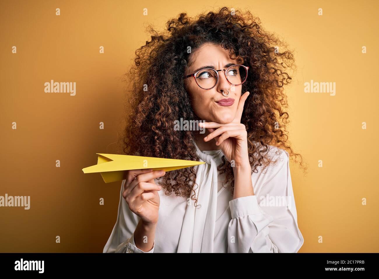 Beautiful woman with curly hair and piercing holding paper plane over ...