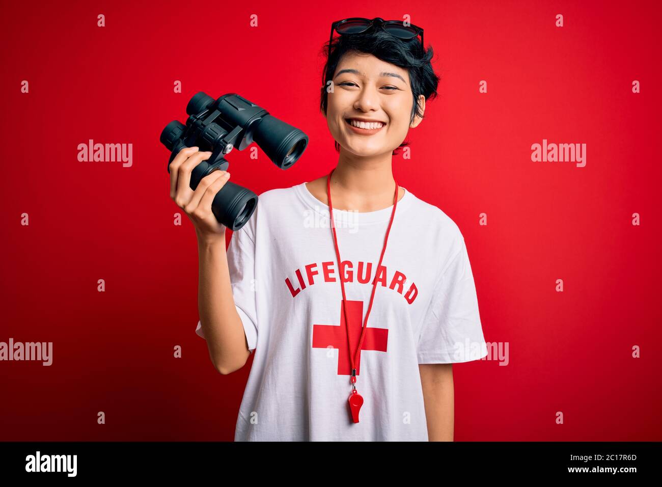 Young beautiful asian lifeguard girl using whistle and binoculars over ...