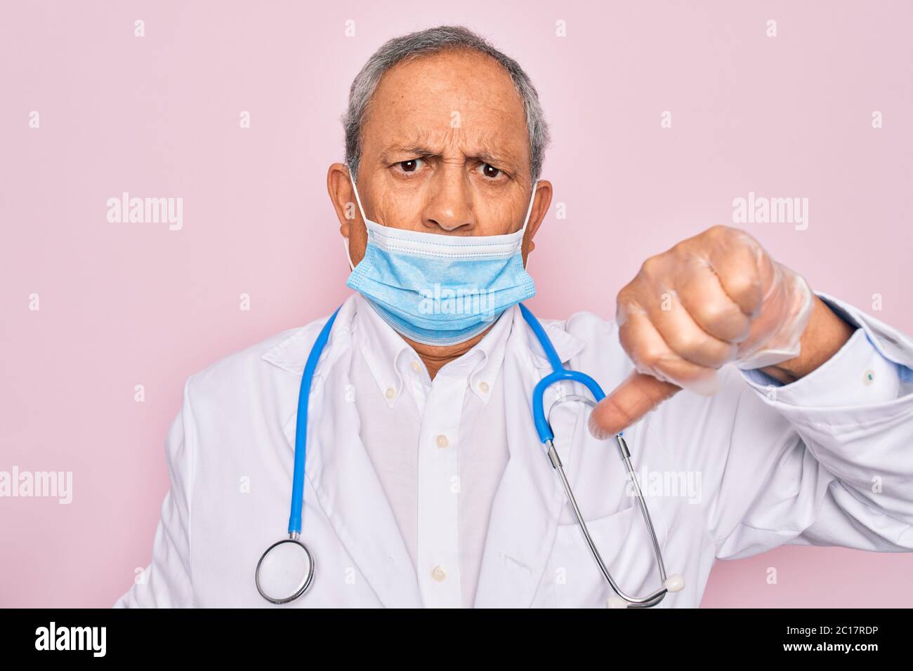 Senior hoary doctor man wearing medical mask and stethoscope over pink ...