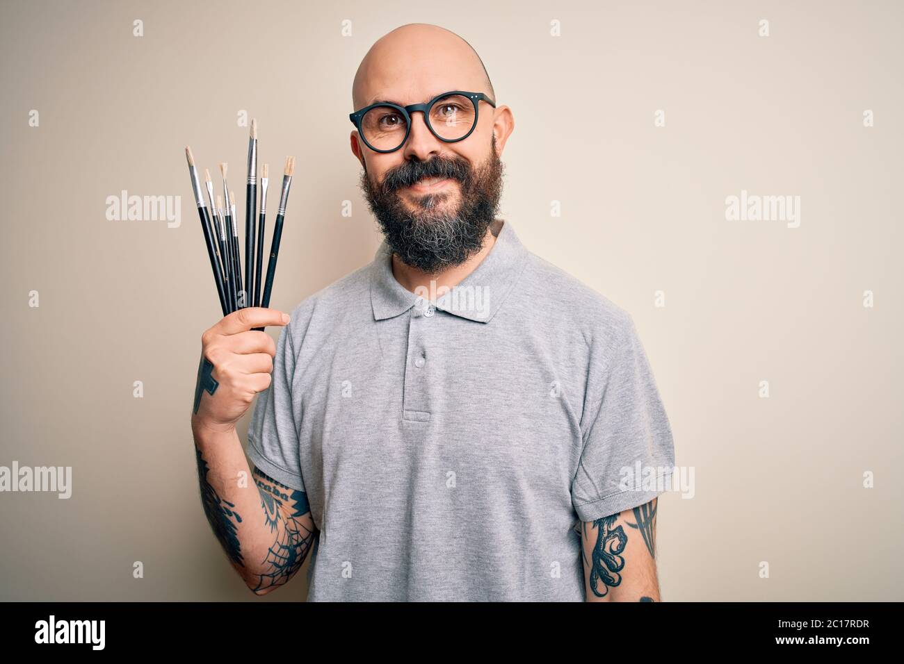 Handsome bald artist man with beard and tattoo painting using painter ...