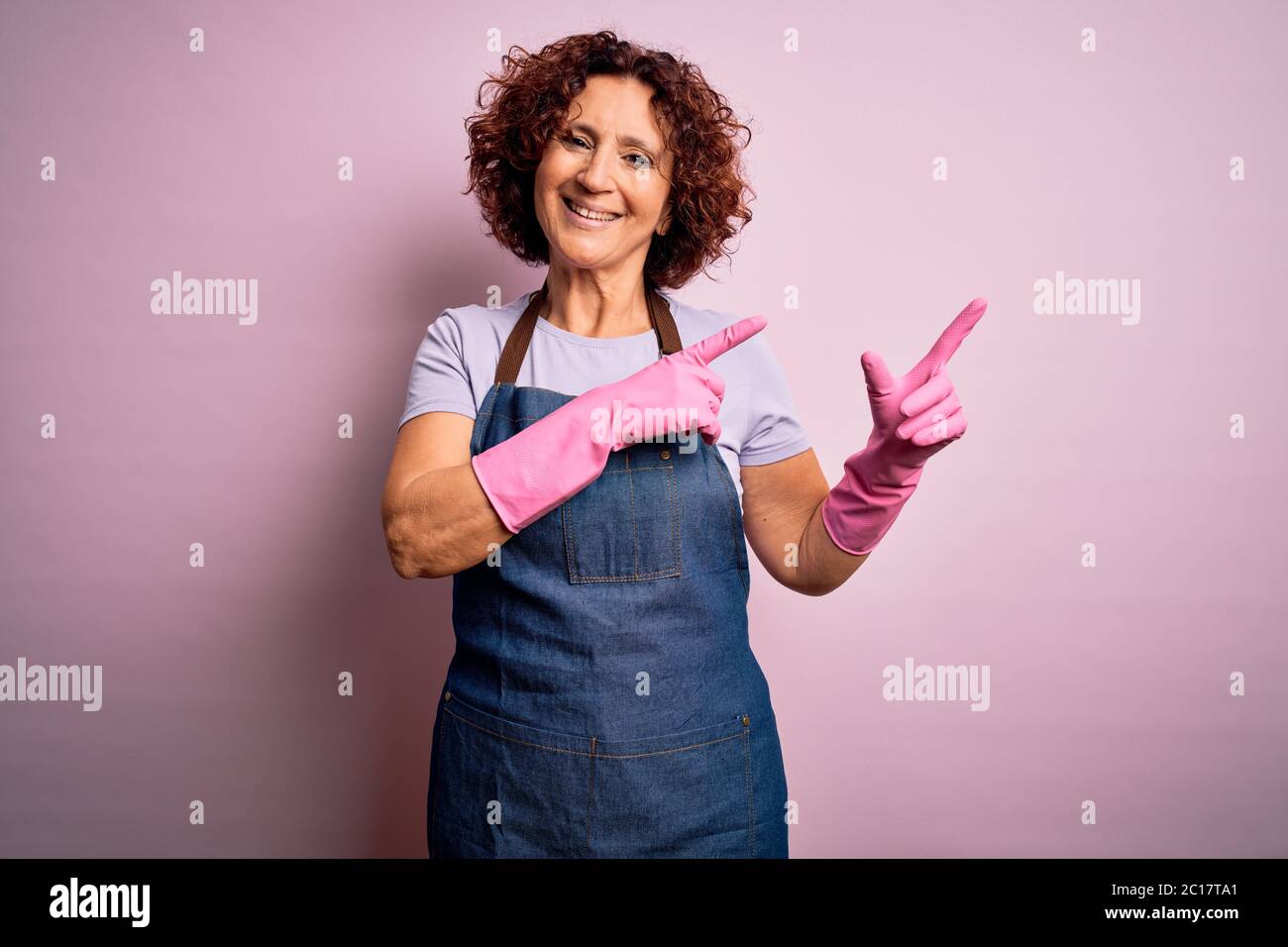 Middle age curly hair woman cleaning doing housework wearing apron and ...