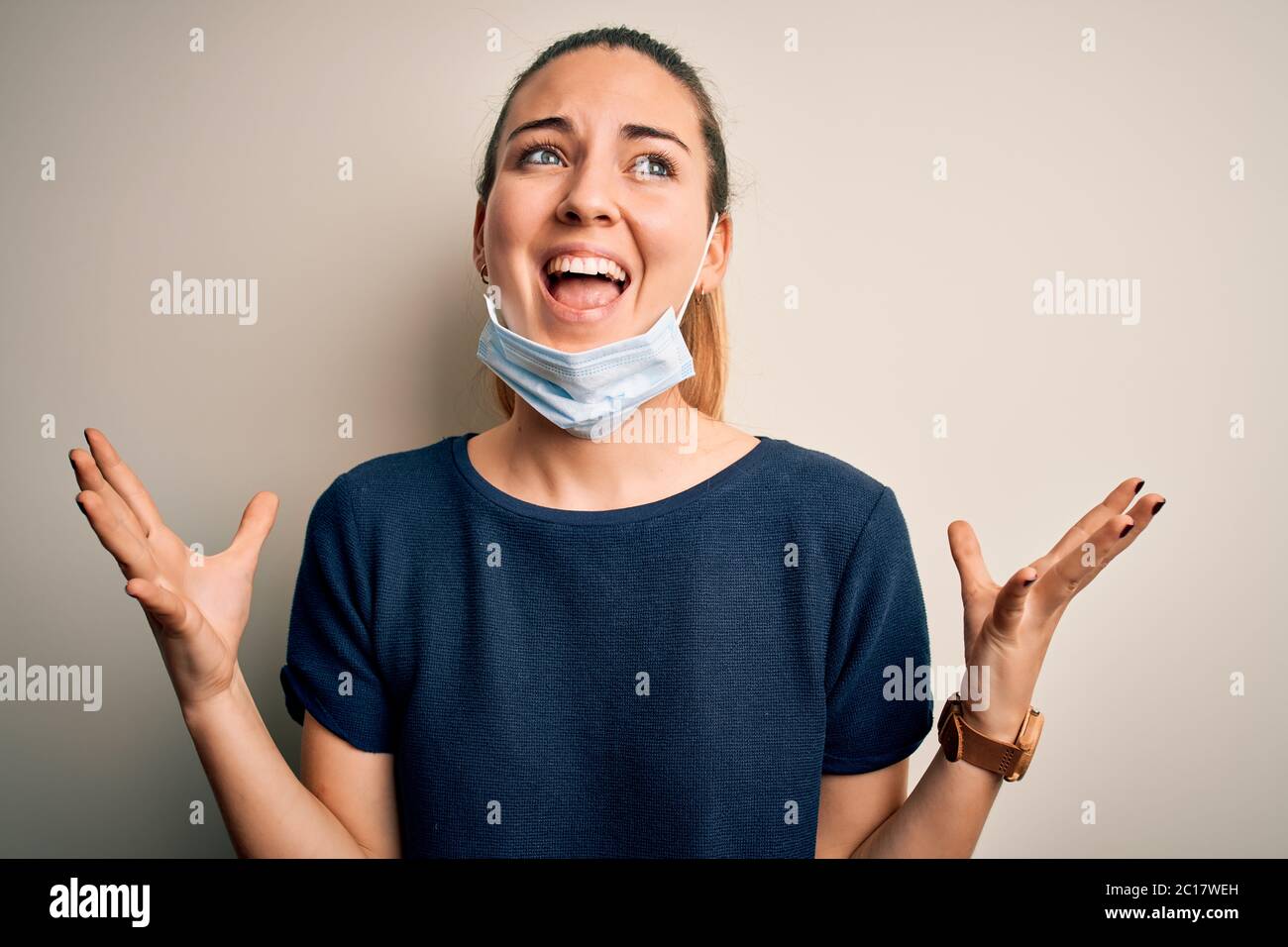 Beautiful blonde woman with blue eyes wearing medical mask over white ...