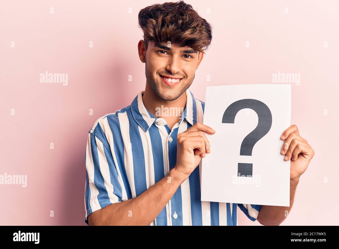 Young hispanic man holding question mark looking positive and happy ...