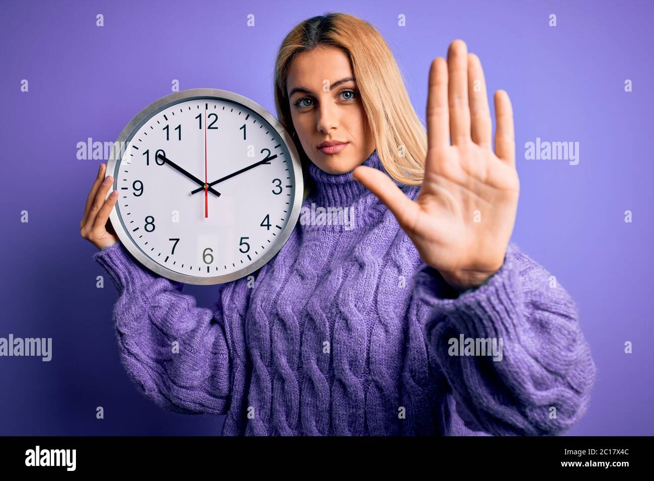 Young beautiful blonde woman doing countdown holding big clock over ...