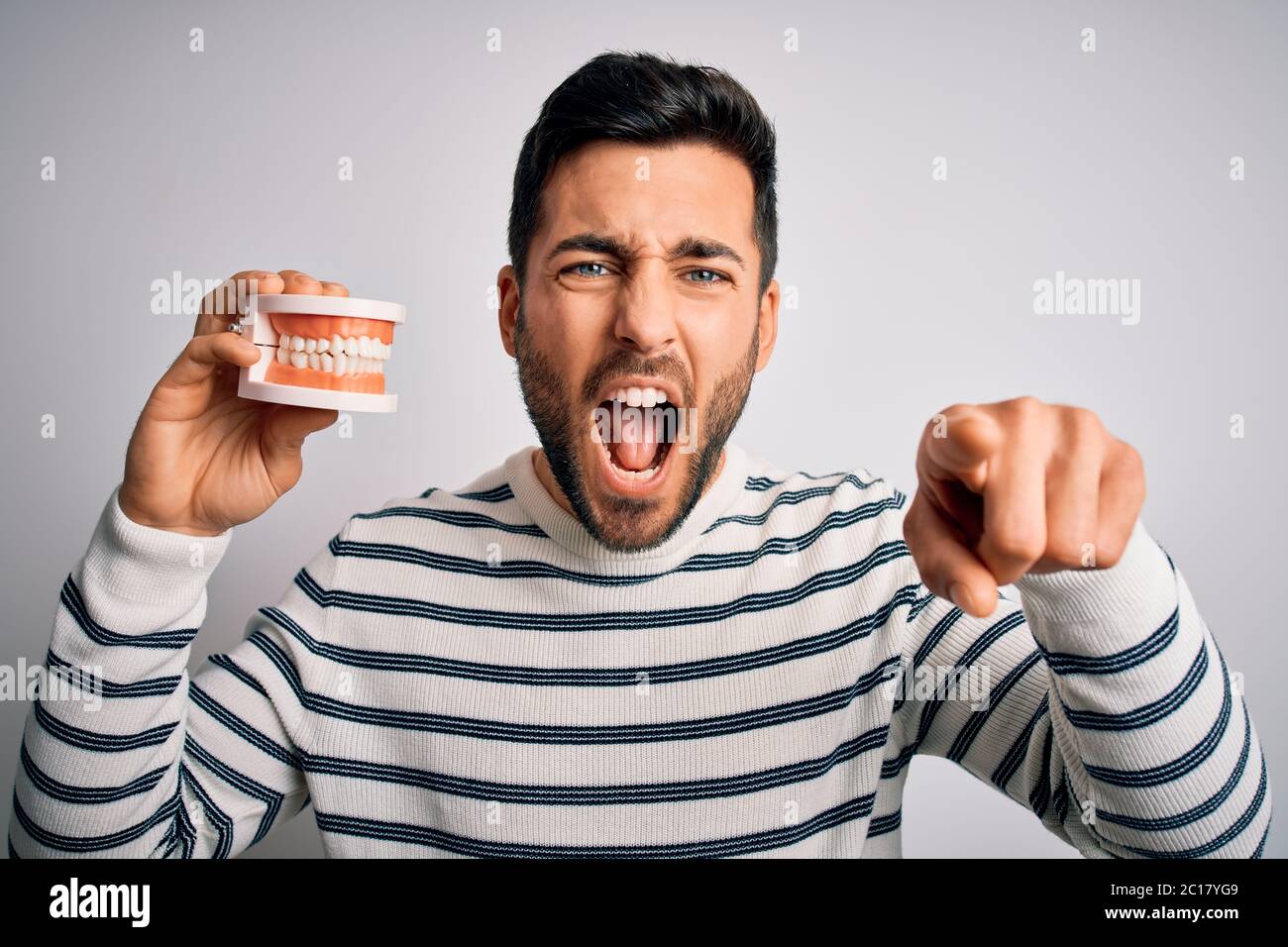 Young handsome man with beard holding plastic denture teeth over white ...