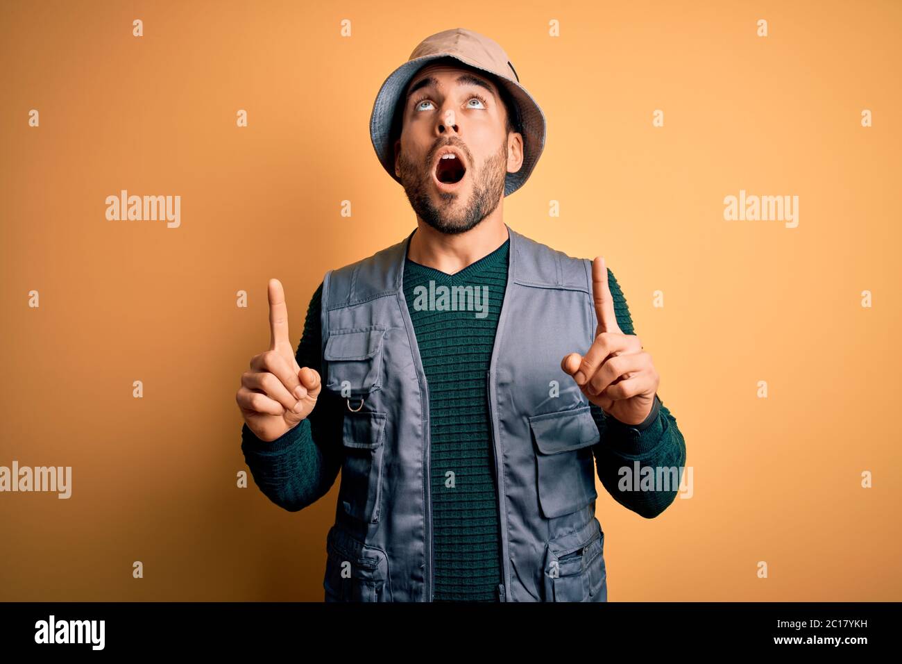 Handsome tourist man with beard on vacation wearing explorer hat over ...