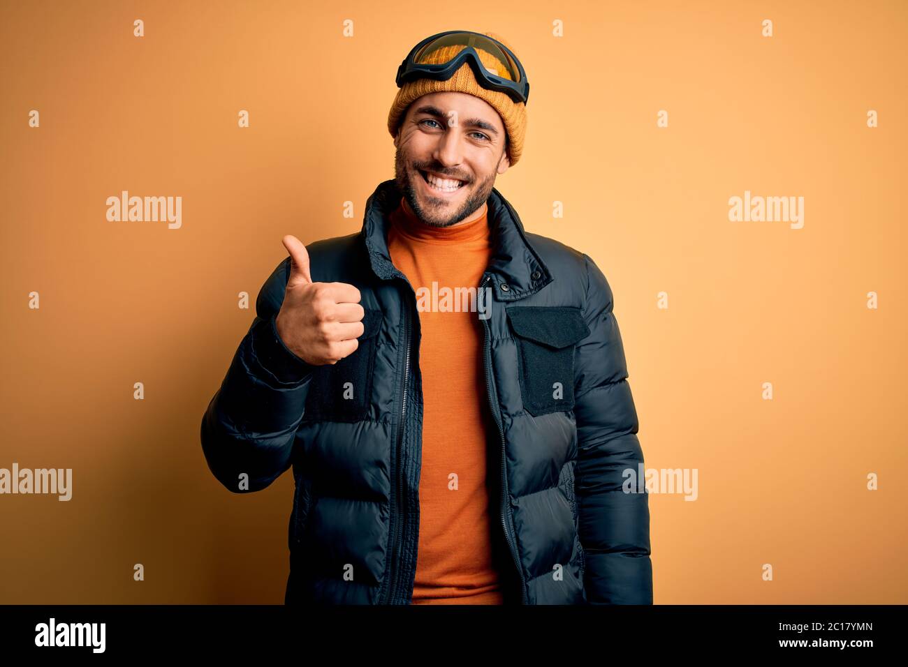 Young handsome skier man with beard wearing snow sportswear and ski ...