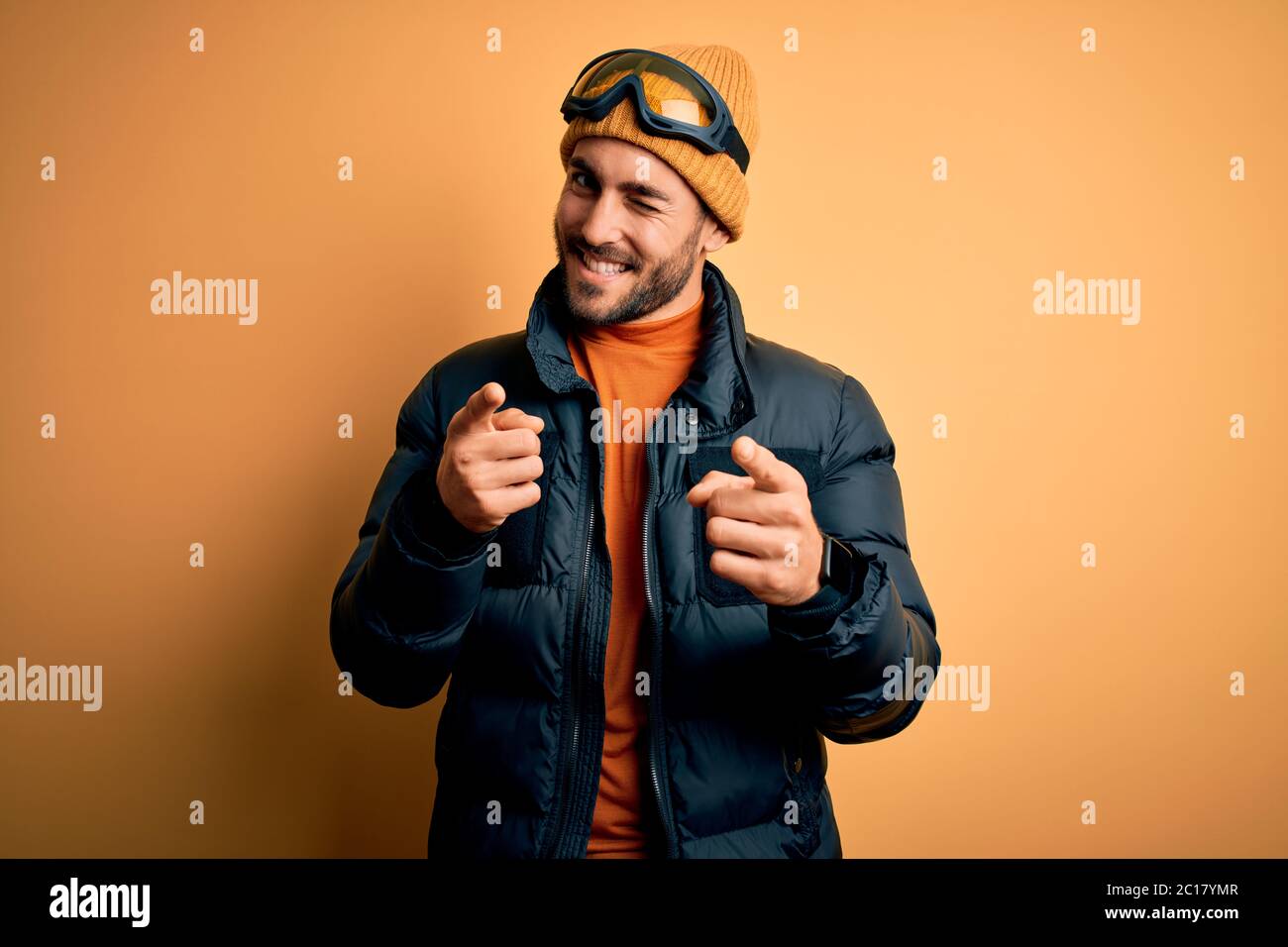 Young handsome skier man with beard wearing snow sportswear and ski ...