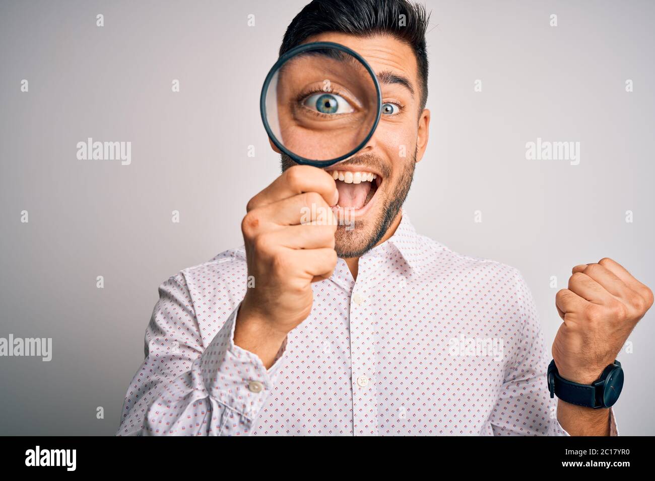 Young detective man looking through magnifying glass over isolated ...