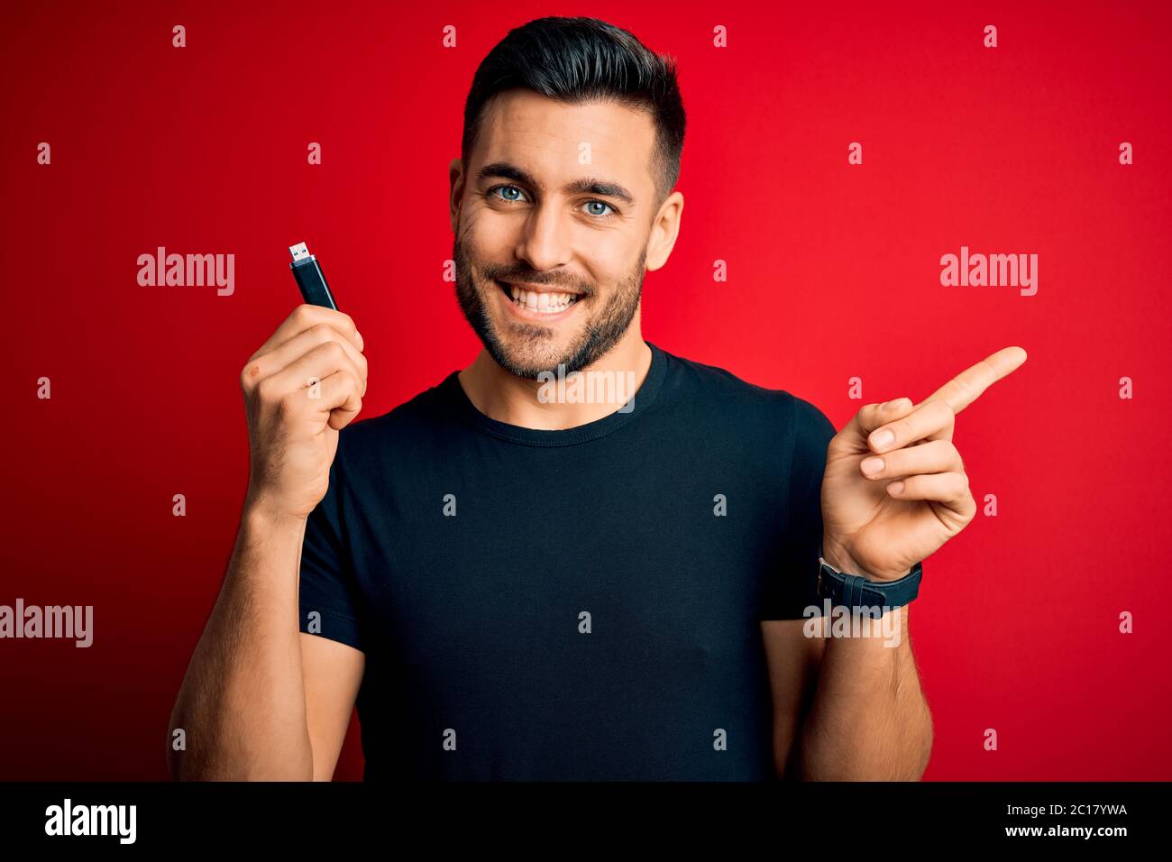 Young man holding USB memory data drive over red isolated background ...