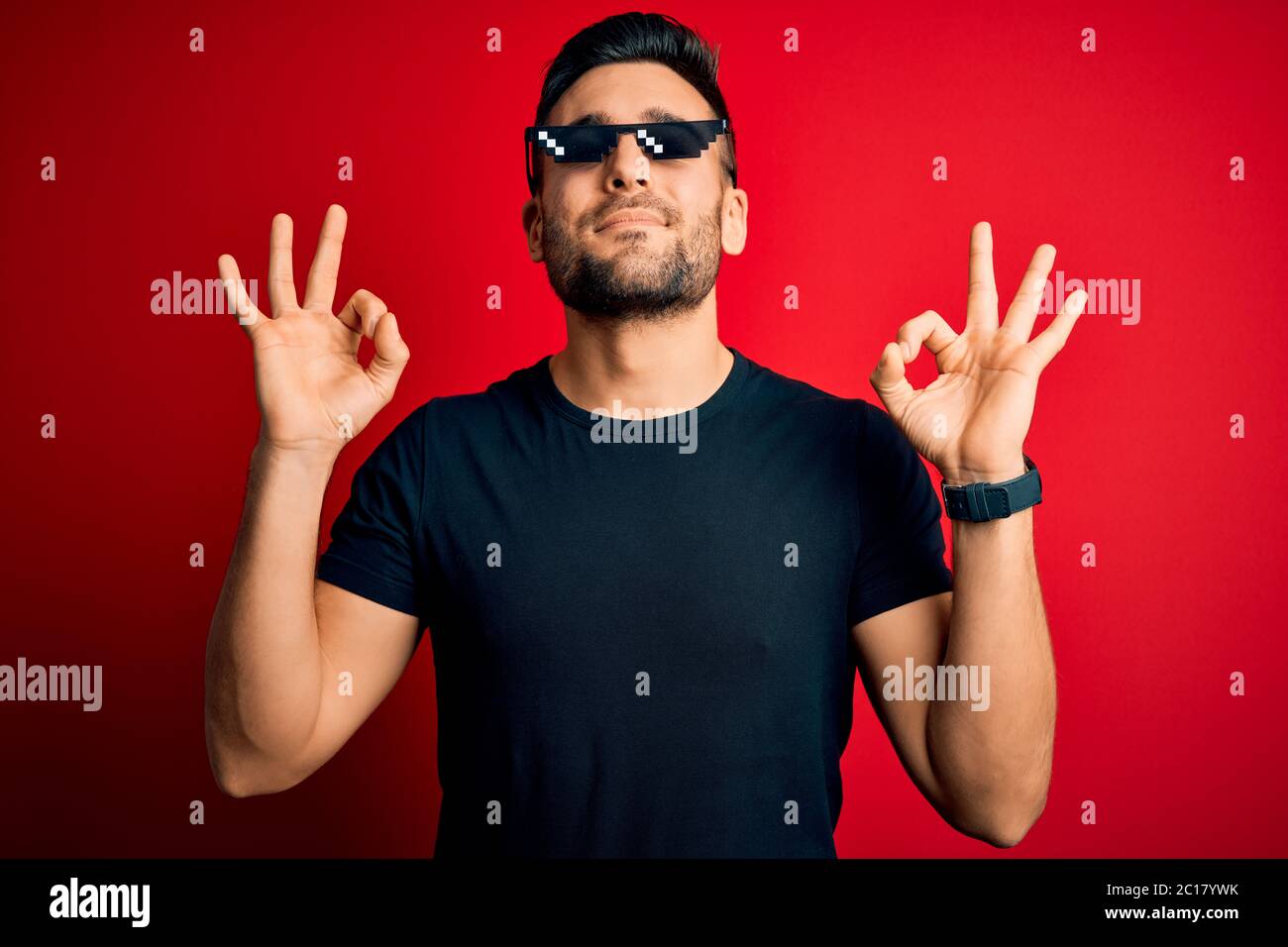 Young handsome man wearing funny thug life sunglasses over isolated red ...