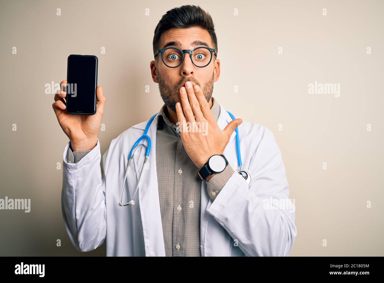 Young doctor man wearing stethoscope showing smartphone screen over ...