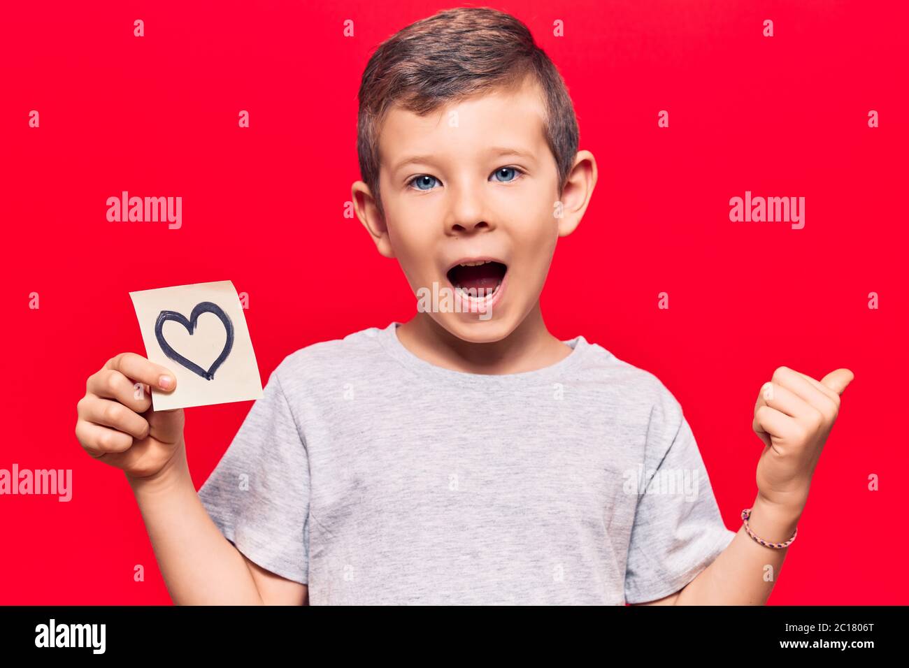 Cute blond kid holding heart reminder pointing thumb up to the side ...