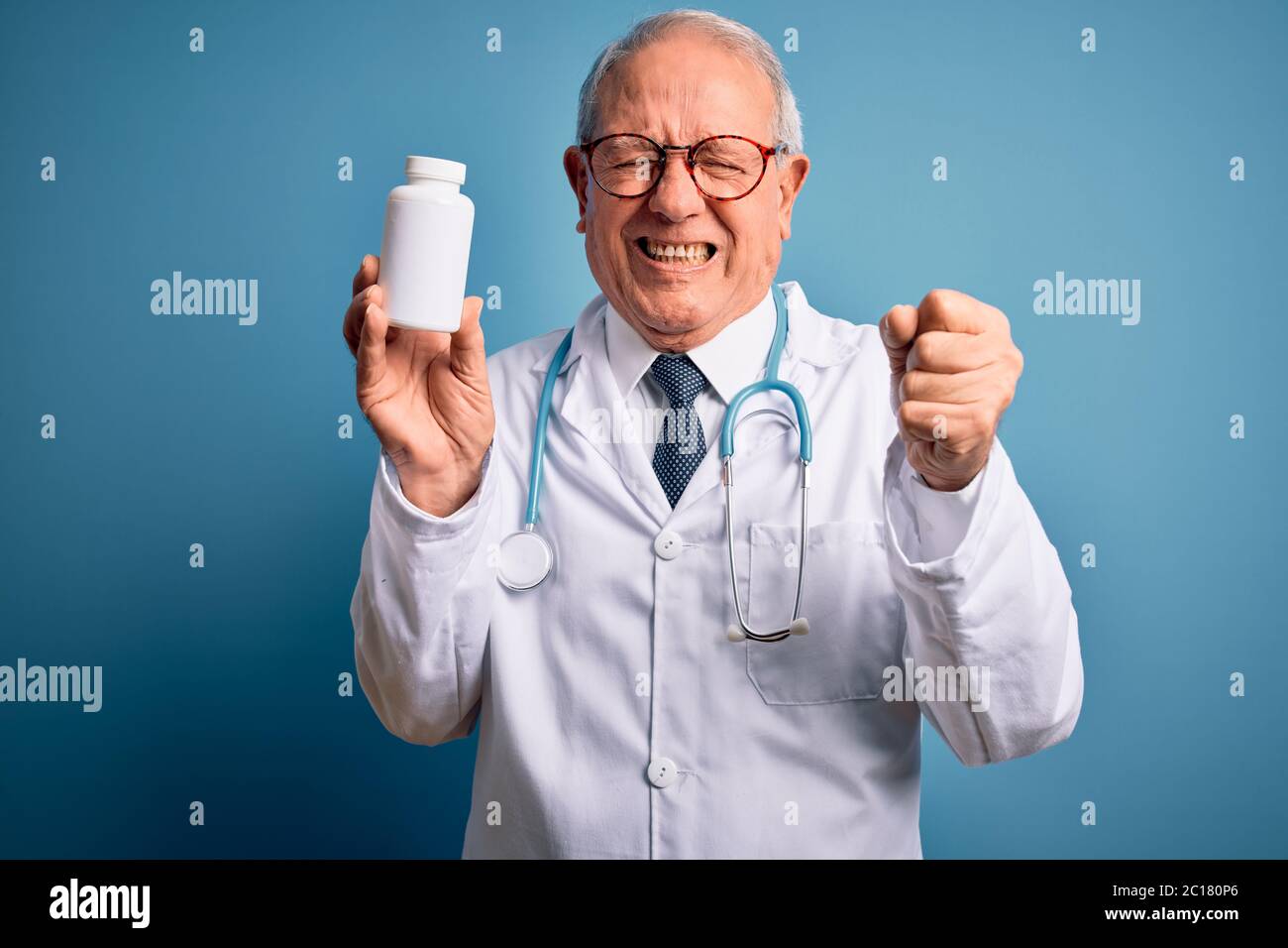 Senior grey haired doctor man holding pharmaceutical pills over blue ...