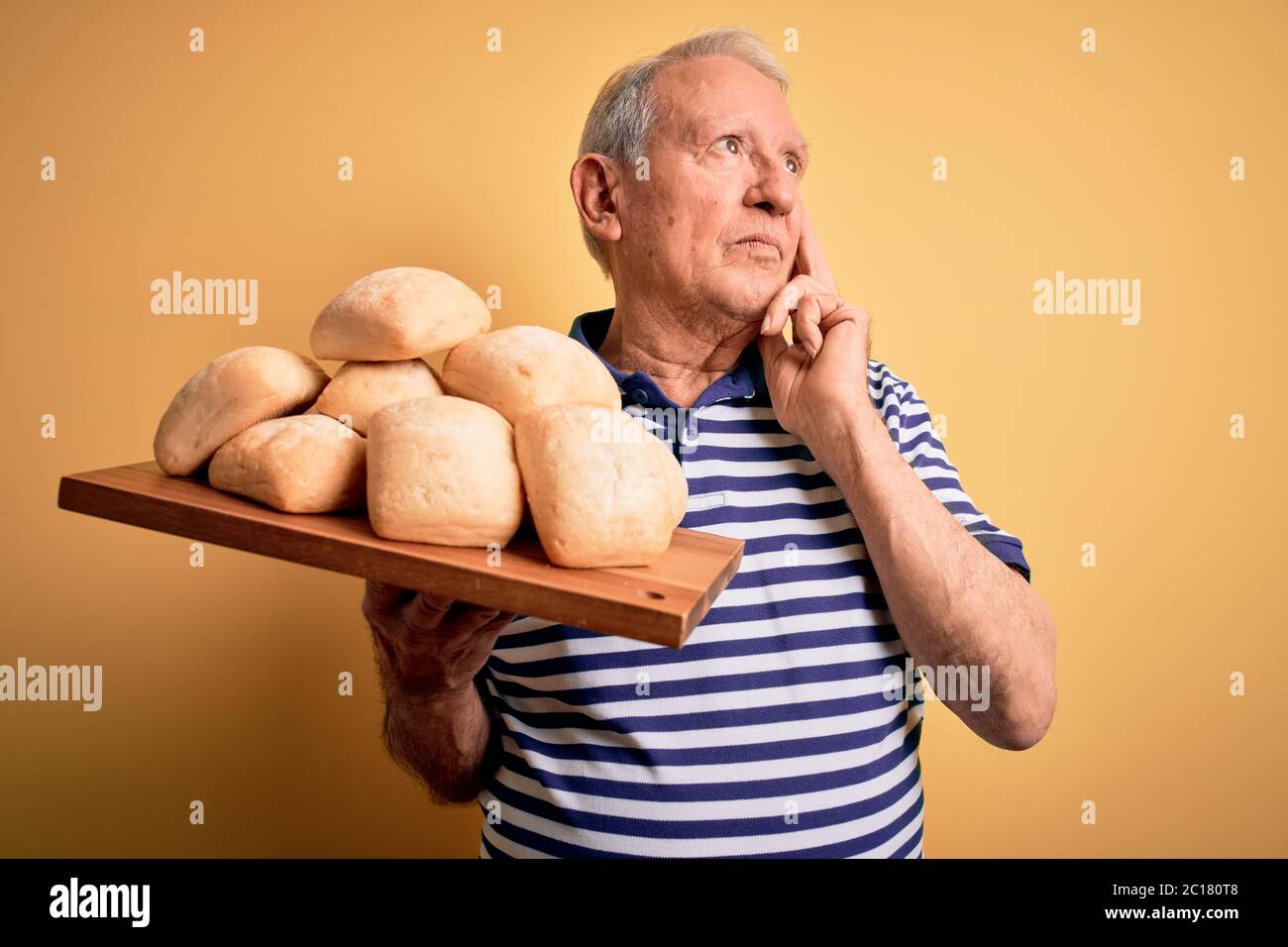 Senior grey haired baker man holding fresh homemade bread over yellow ...