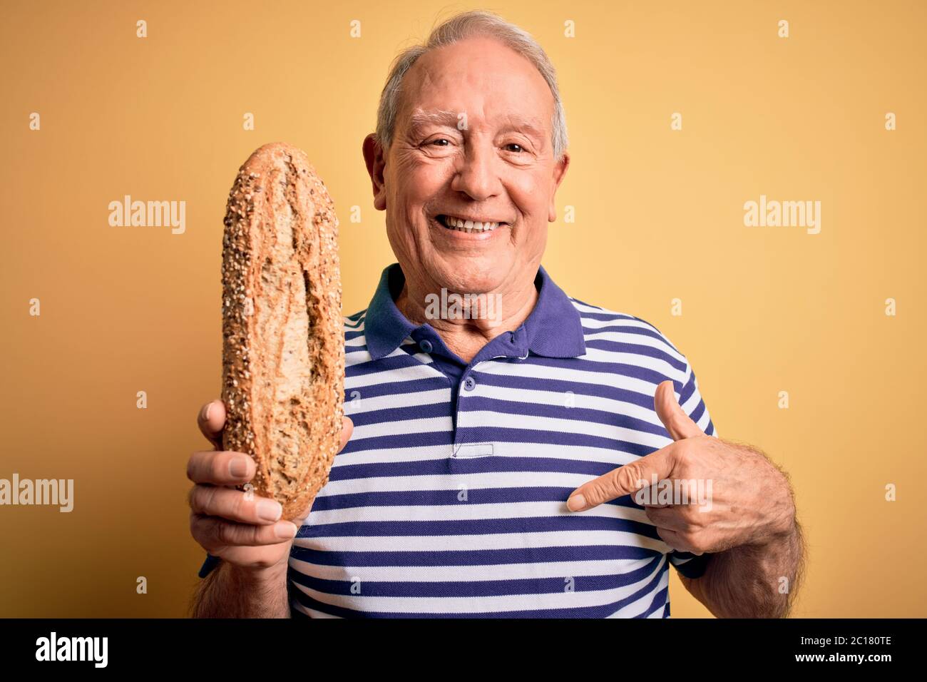 Grey haired senior man holding healthy wholemeal bread over yellow ...