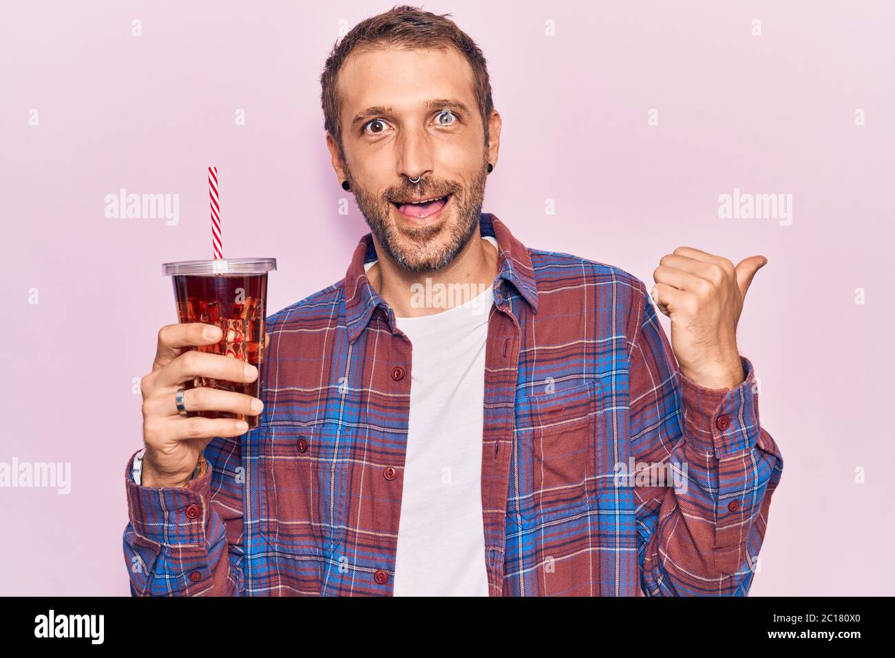 Young handsome man drinking glass of cola beverage pointing thumb up to ...