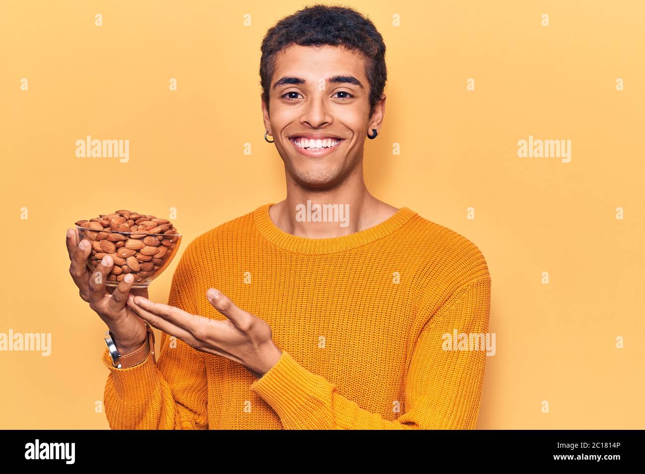 Young african amercian man holding bowl with almonds looking positive ...