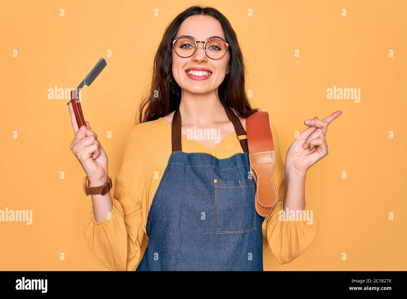 Young beautiful barber woman wearing apron holding razor blade over ...