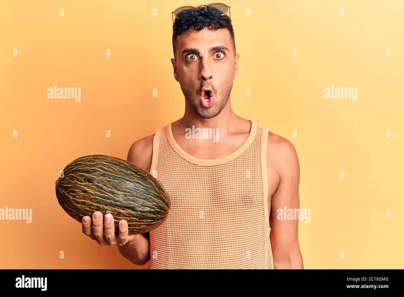 Young hispanic man holding melon scared and amazed with open mouth for ...
