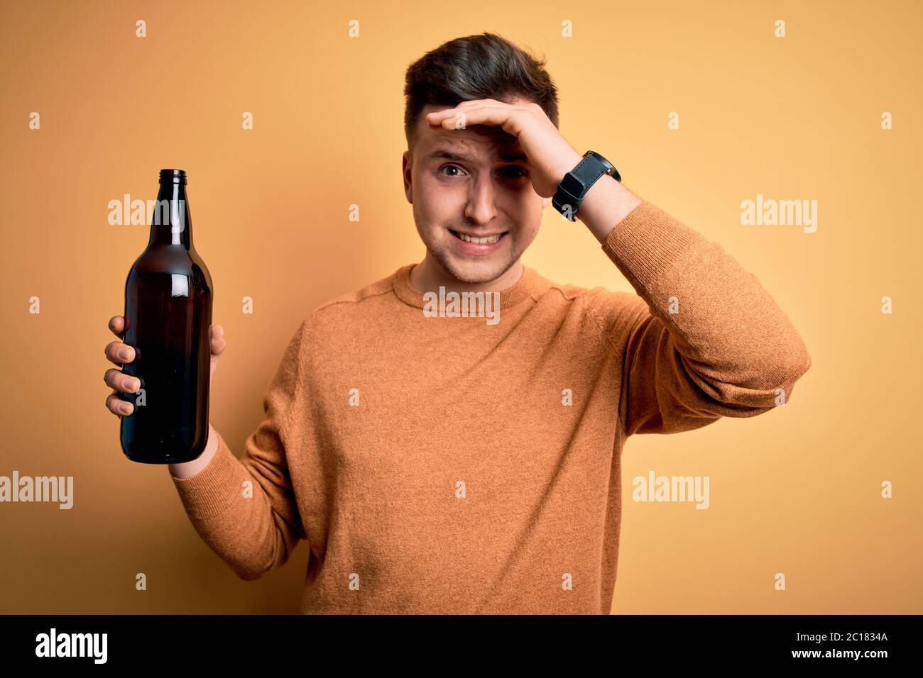 Young handsome caucasian man drinking a bottle of beer over yellow ...