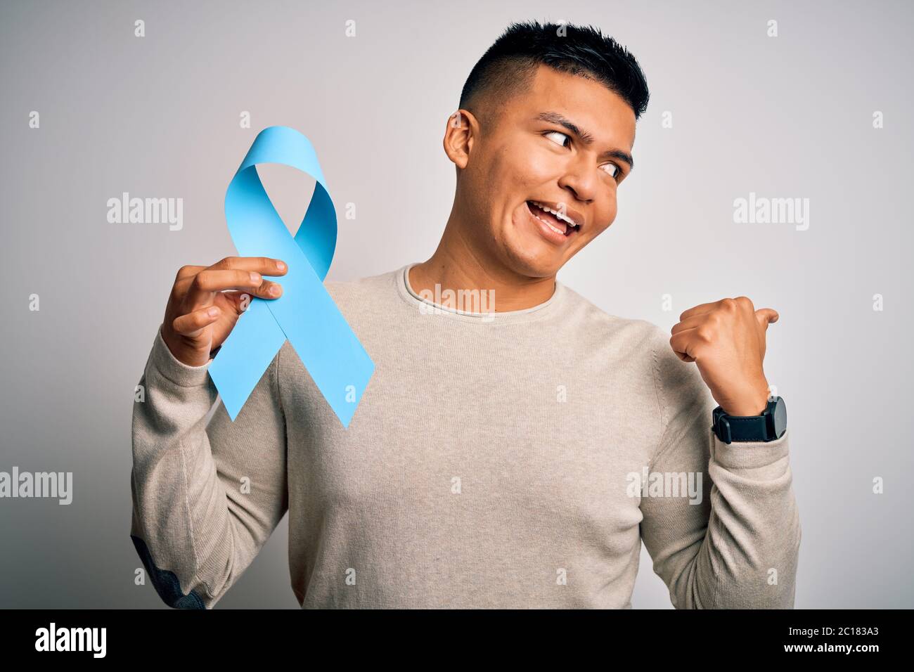 Young handsome latin man holding blue cancer ribbon over isolated white ... Young handsome latin man holding blue cancer ribbon over isolated white ...