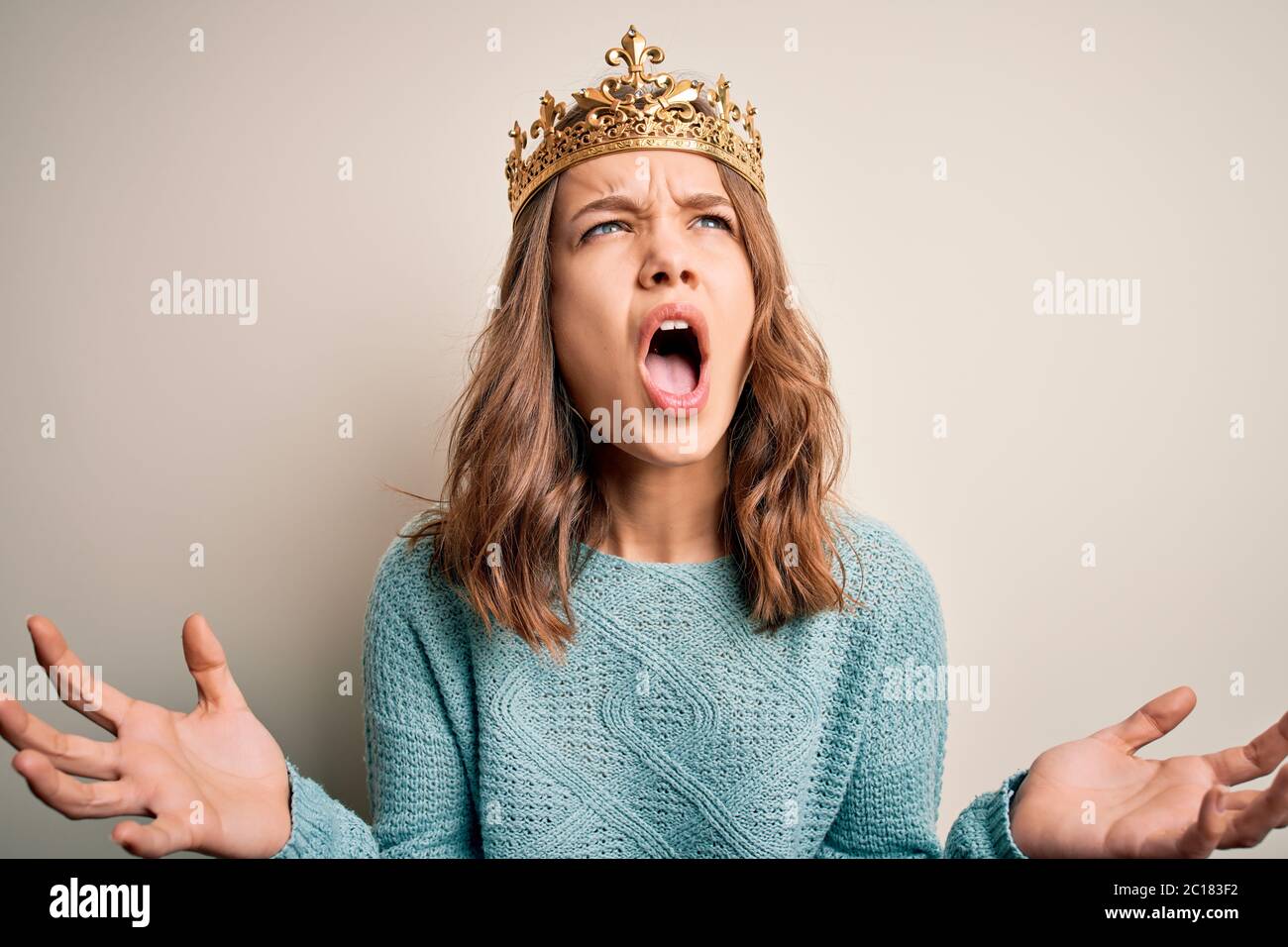 Young blonde girl wearing queen golden crown over isolated background ...