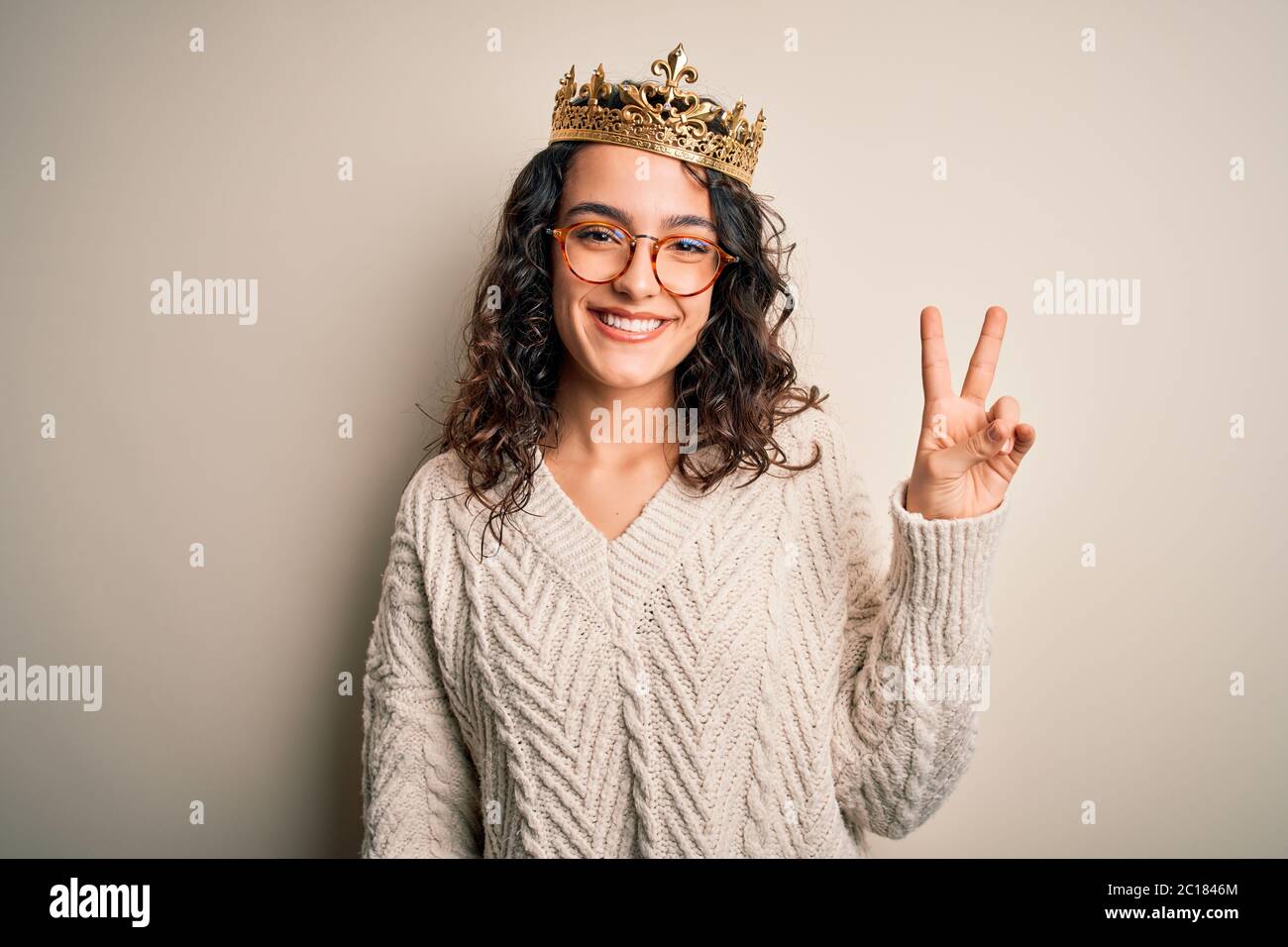 Young beautiful woman with curly hair wearing golden queen crown over ...