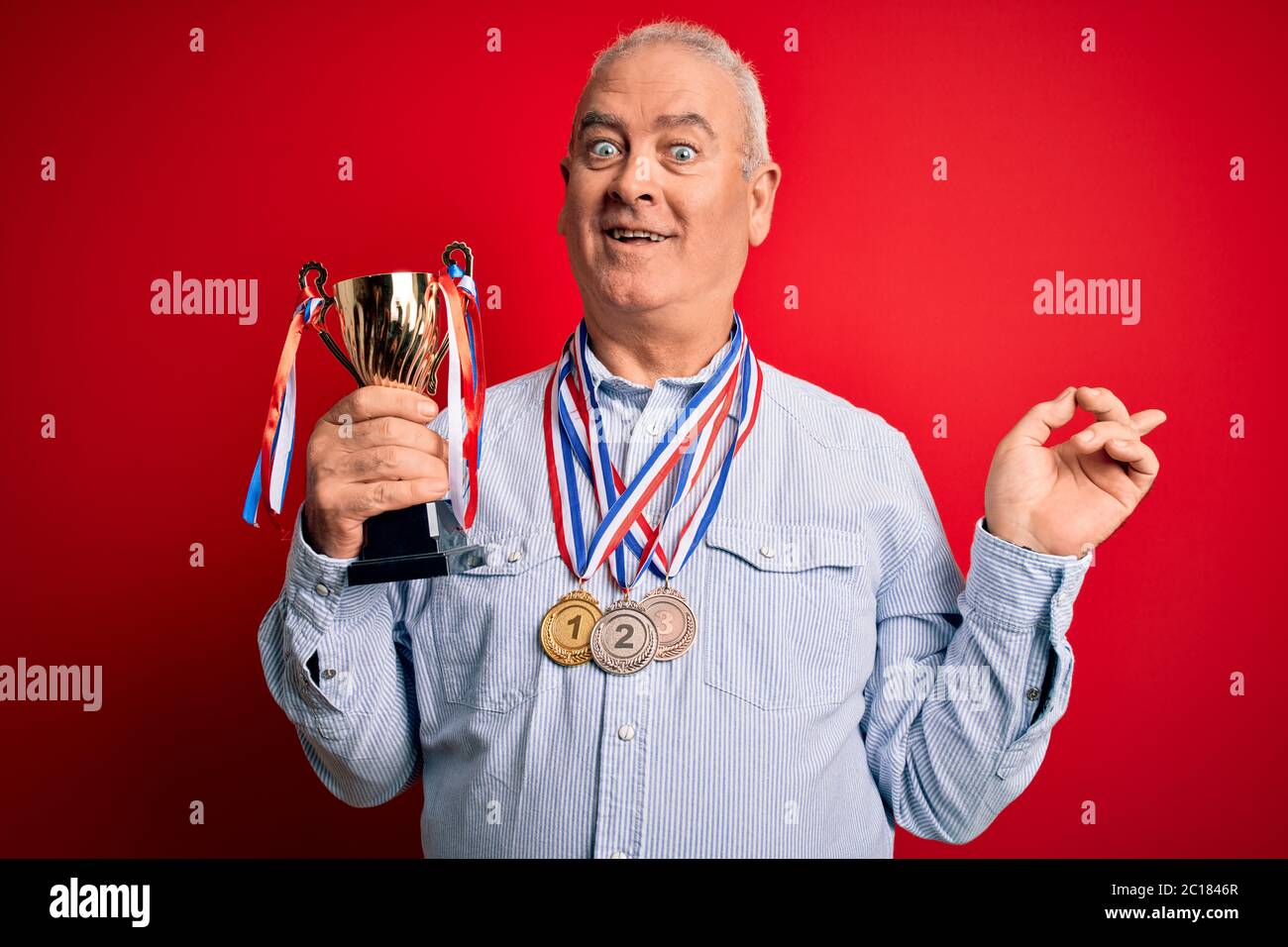 Middle age hoary successful man wearing medals holding trophy over ...