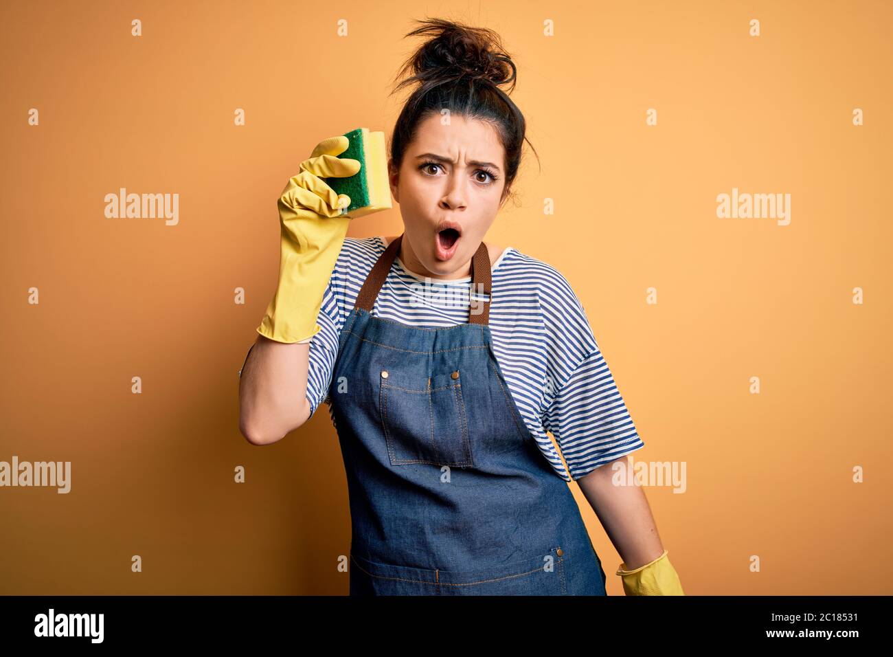 Young brunette cleaner woman wearing housekeeping gloves holding ...