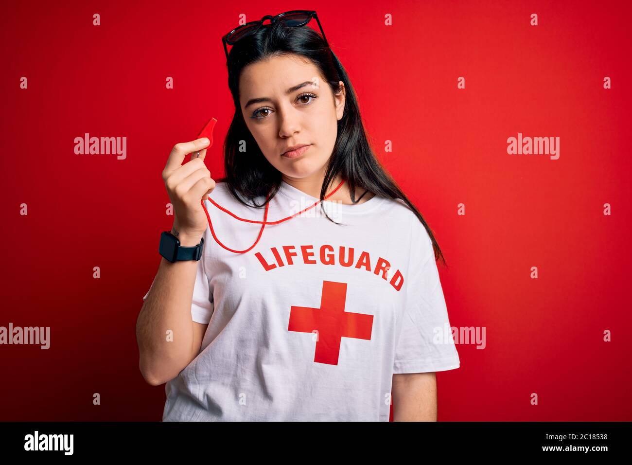 Young lifeguard woman wearing guard equipement holding whistle over red ...
