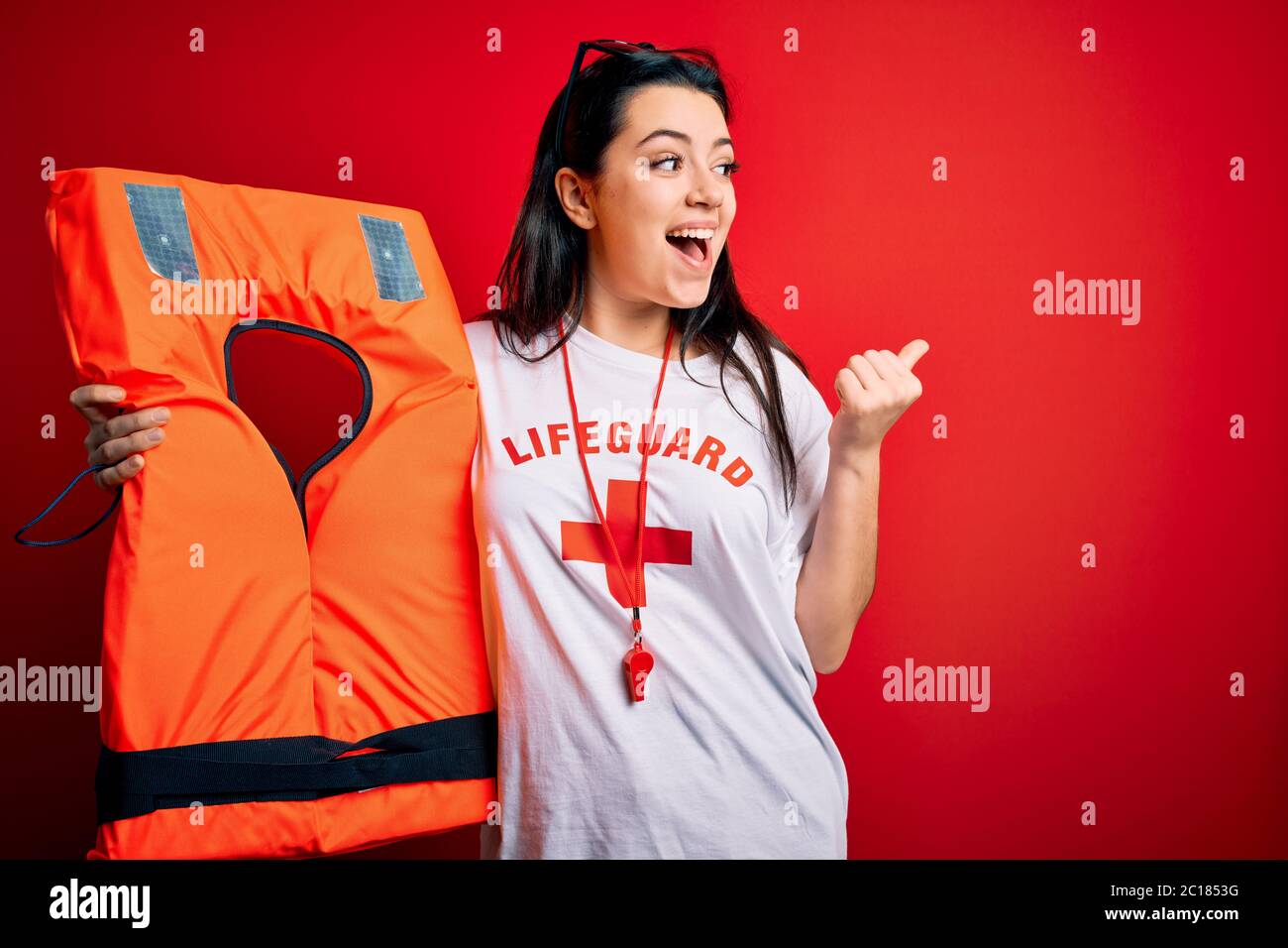 Young lifeguard woman holding rescue lifejacket over red background ...