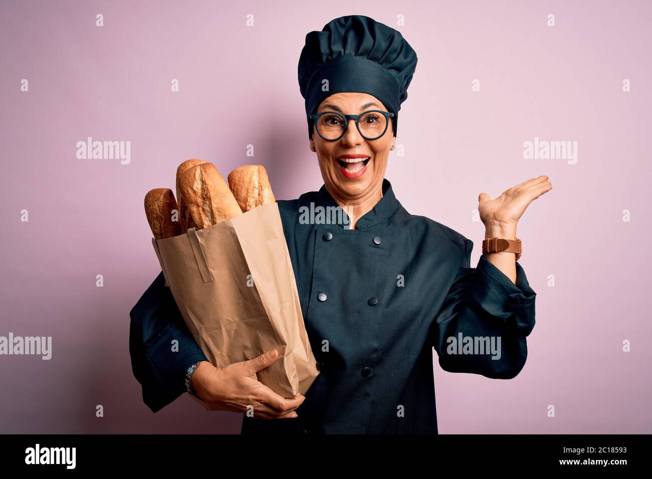 Middle age baker woman wearing cooker uniform and hat holding paper bag ...