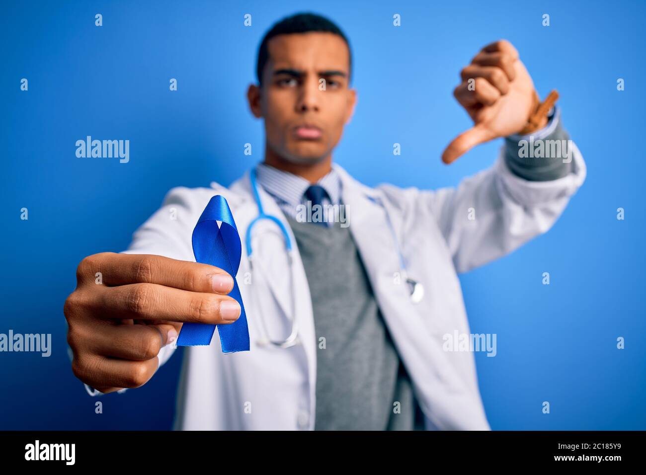 Young handsome african american doctor man holding blue cancer ribbon ...