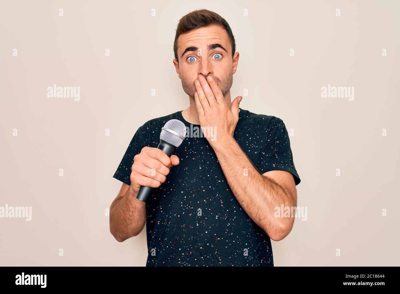 Young handsome singer man with blue eyes singing using microphone over white background cover ...