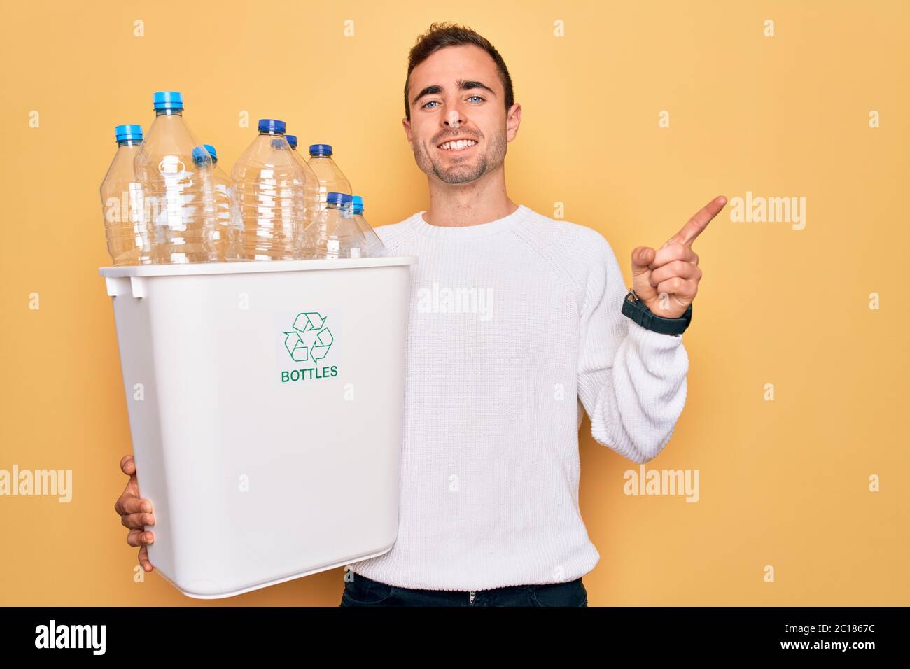 Young handsome man with blue eyes recycling holding wastebasket with ...
