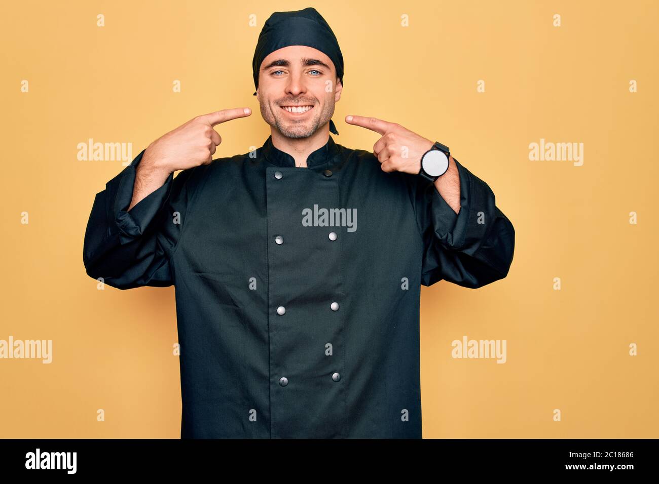 Young handsome cooker man with blue eyes wearing uniform and hat over ...