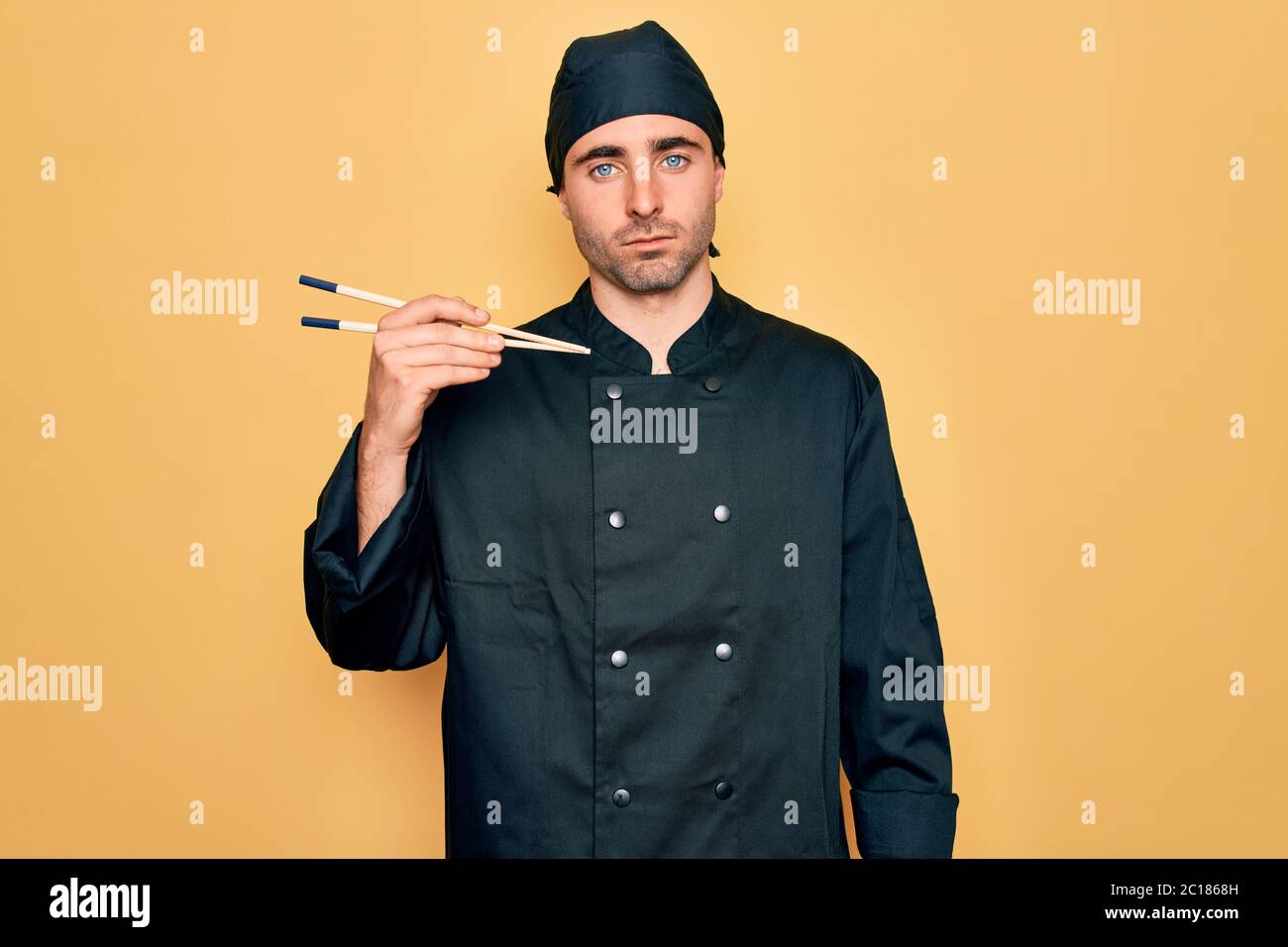Young handsome cooker man with blue eyes wearing uniform and hat using ...