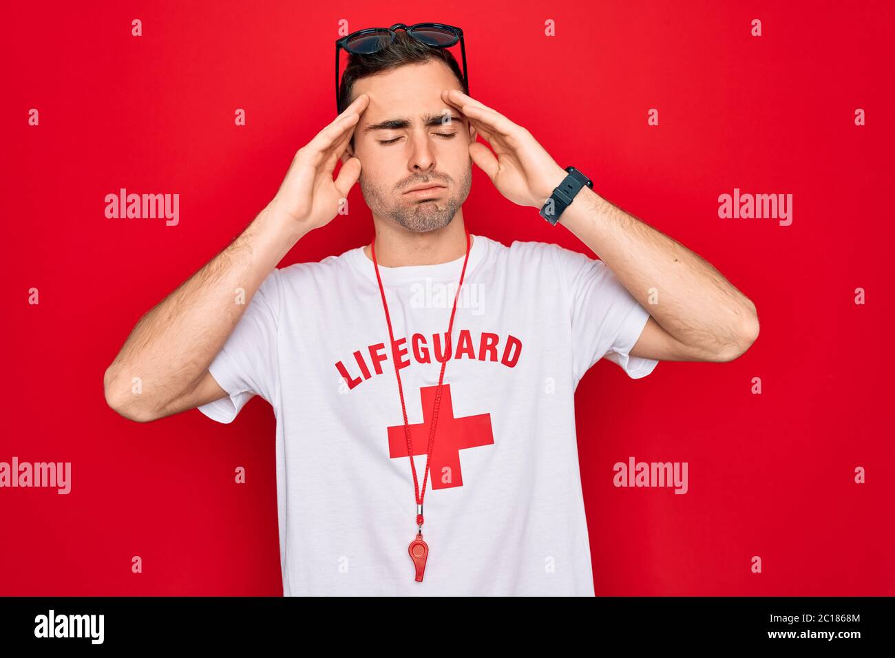 Handsome lifeguard man wearing t-shirt with red cross and whistle over ...