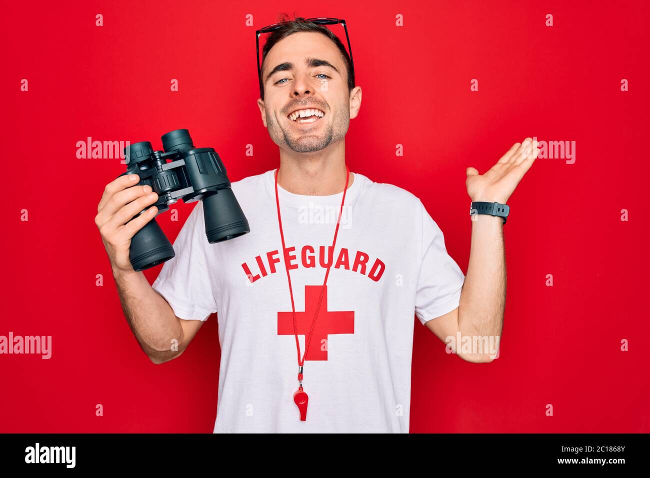 Young handsome lifeguard man wearing t-shirt with red cross and whistle ...