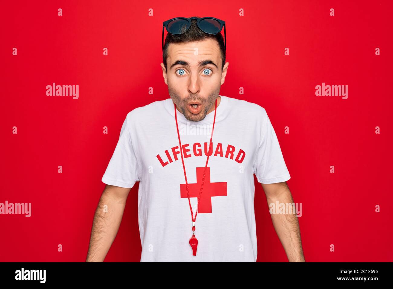 Handsome lifeguard man wearing t-shirt with red cross and whistle over ...