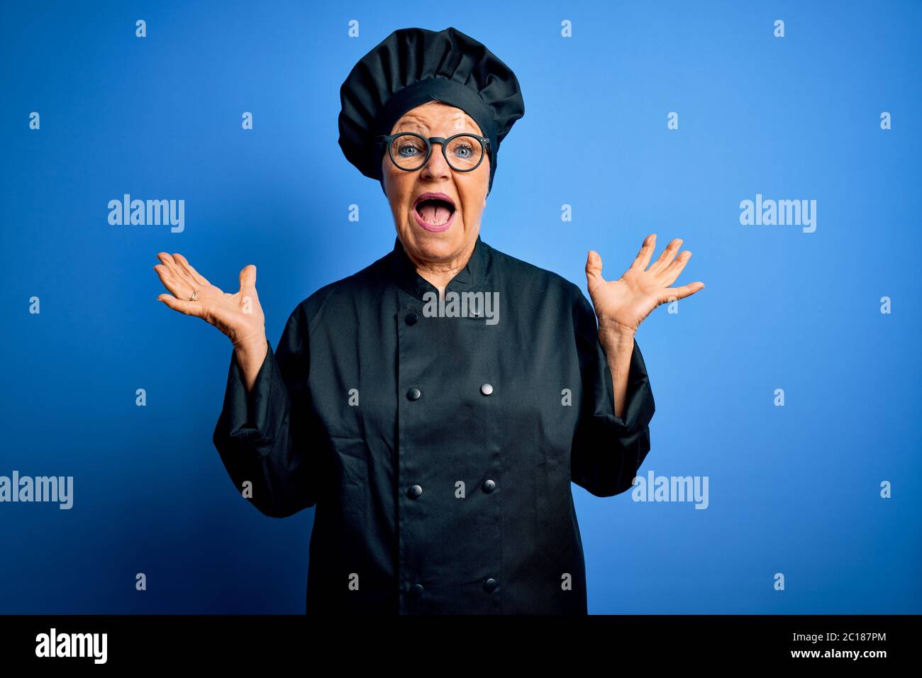 Senior beautiful grey-haired chef woman wearing cooker uniform and hat ...