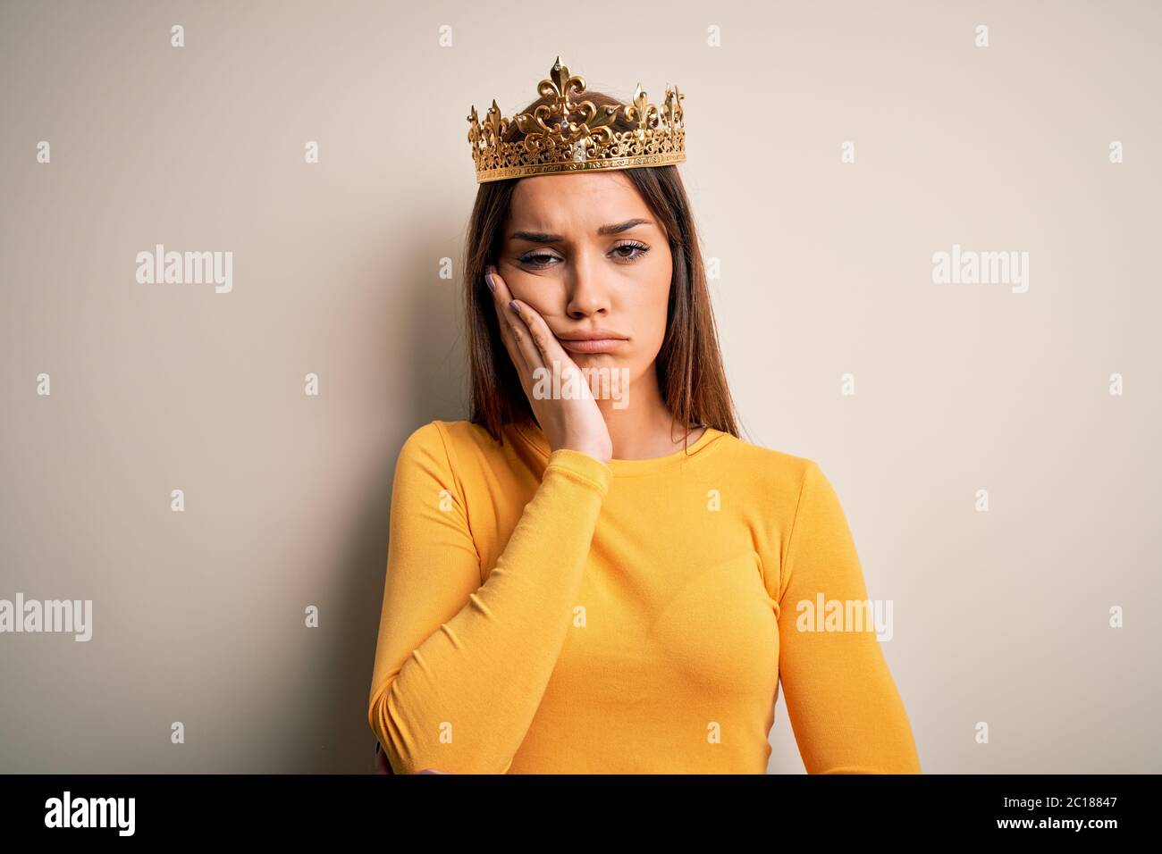 Young beautiful brunette woman wearing golden queen crown over white ...