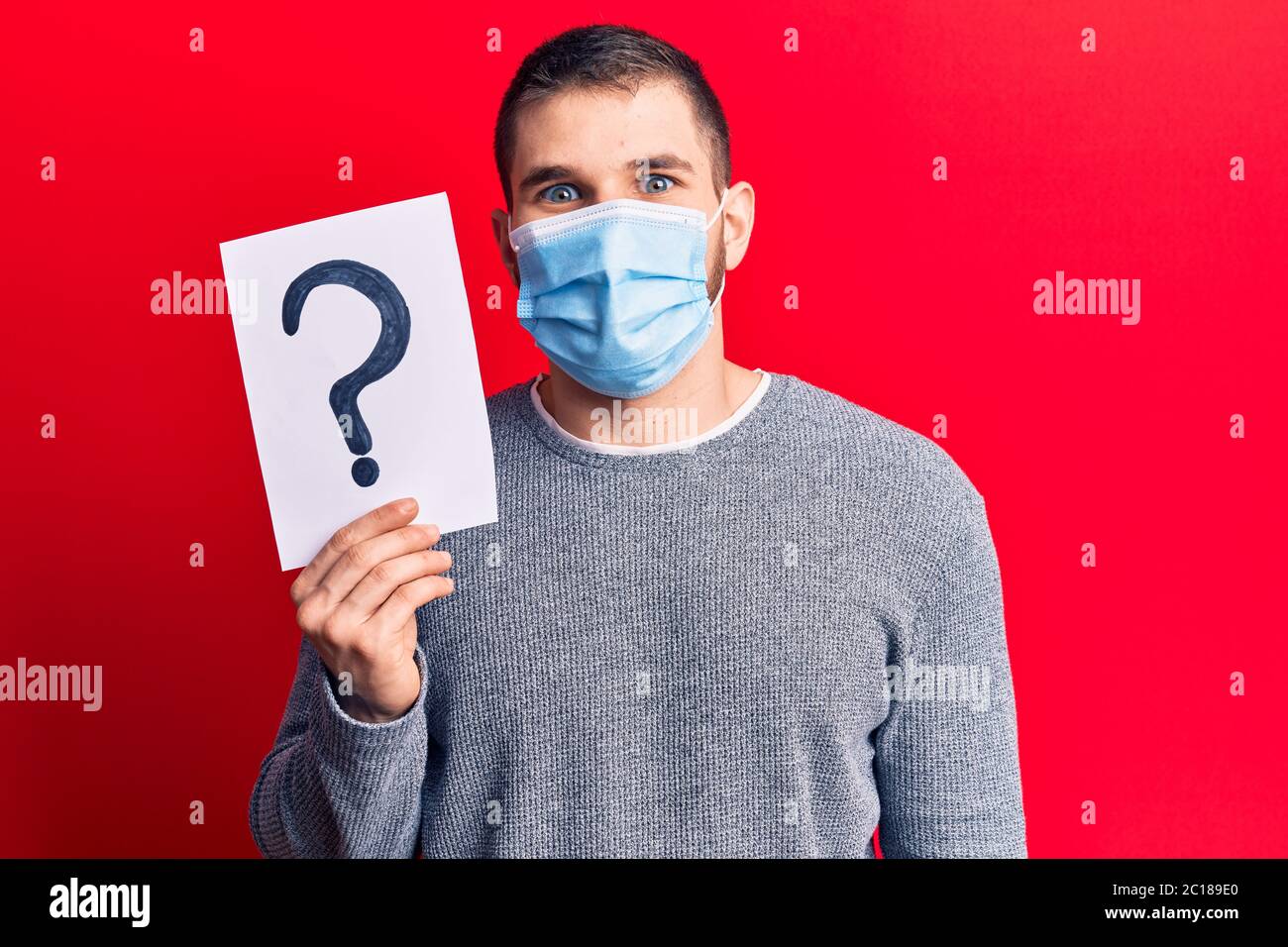 Young handsome man wearing medical mask holding question mark looking ...