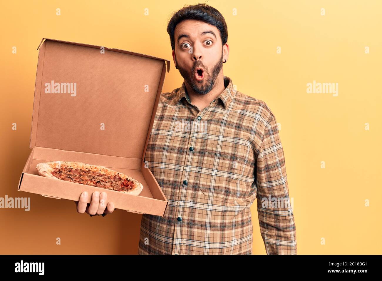 Young hispanic man holding delivery pizza box scared and amazed with ...