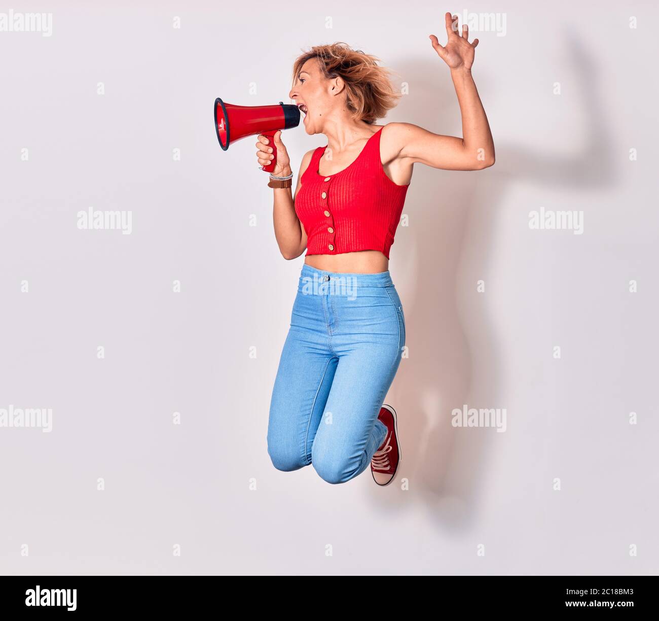 Young beautiful caucasian woman screaming using megaphone. Jumping over ...