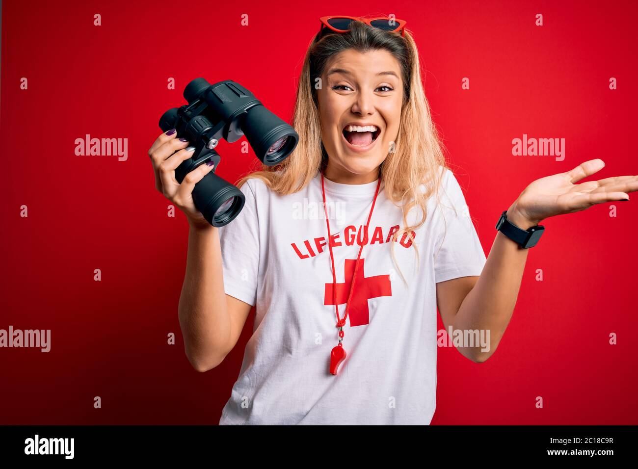 Young beautiful blonde lifeguard woman using binoculars and whistle ...