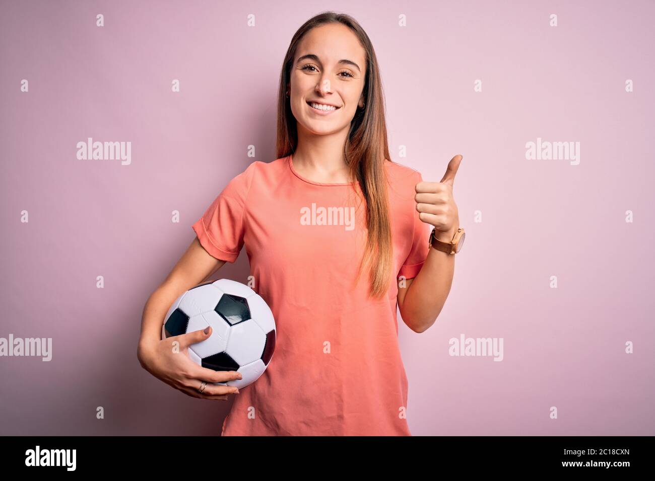 Young beautiful player woman playing soccer holding football ball over ...