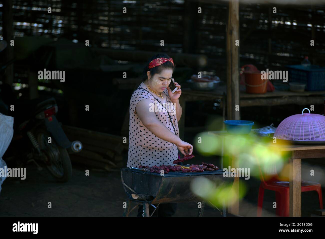 An indigenous, ethnic Shan woman on her mobile phone, grilling meat in ...