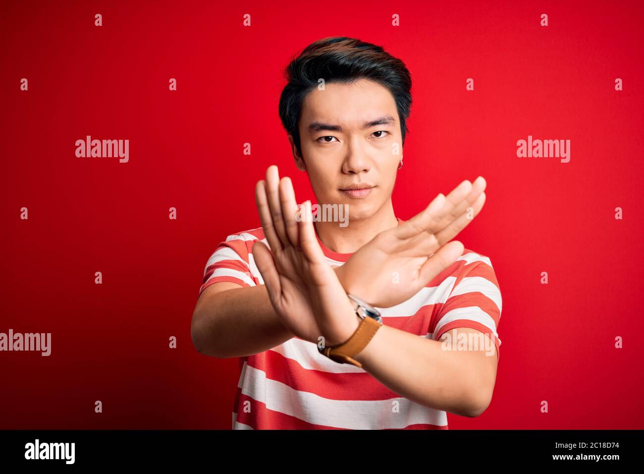 Young handsome chinese man wearing casual striped t-shirt standing over ...